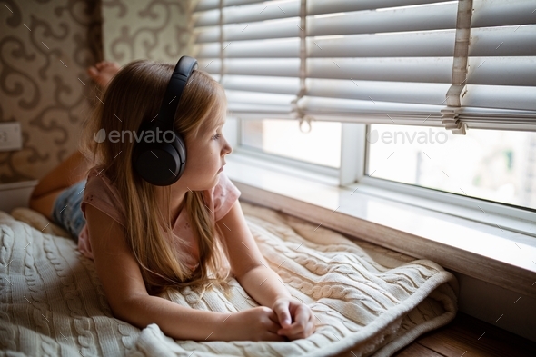 Sad kid listening music via wireless headphones at home when relaxing ...