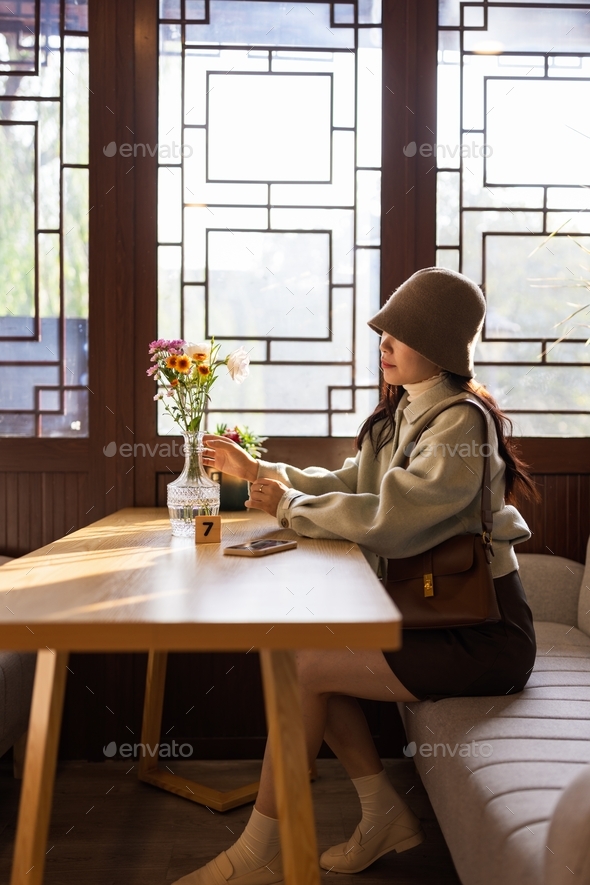 Happy stylish young asian generation z woman waiting coffee in small cafeteria at fall season ...