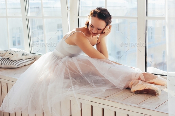 Candid portrait of Ballet dancer ballerina in light blue dress smiling sitting on window sill ...
