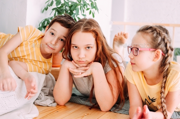 Three cute smiling children friends tweens lying on the floor at home ...
