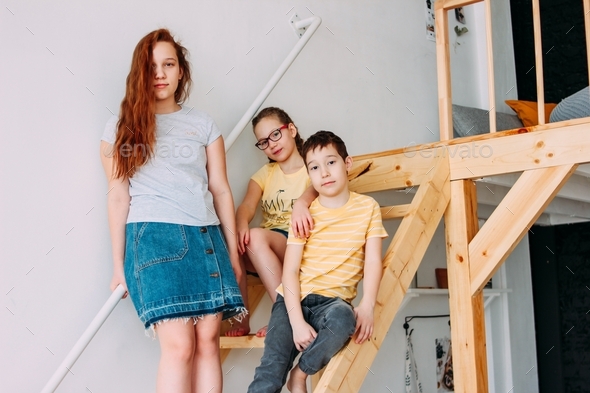 Three cute smiling children friends tweens lying on the stairs at home ...