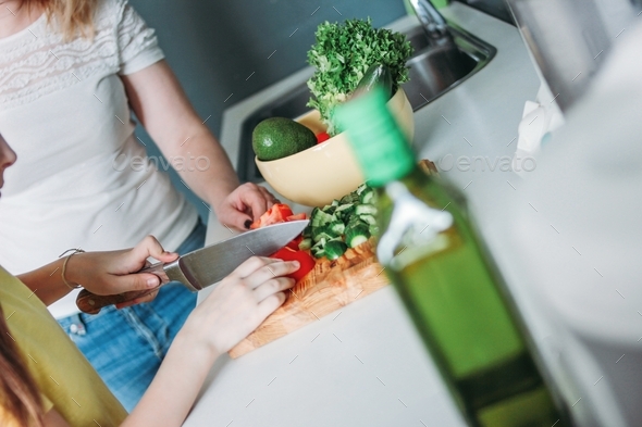 Tween girl and her mother making vegetable salad in the kitchen at home ...