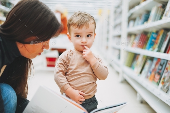 Cute baby boy toddler child in bookstore with mother with open book ...