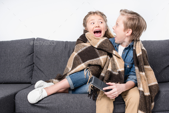 scared kids in blanket sitting on sofa and looking at each other ...