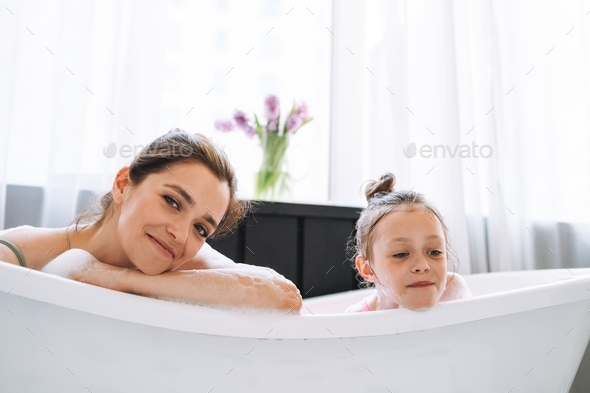 Young mother with little daughter having fun in bath with foam at home ...