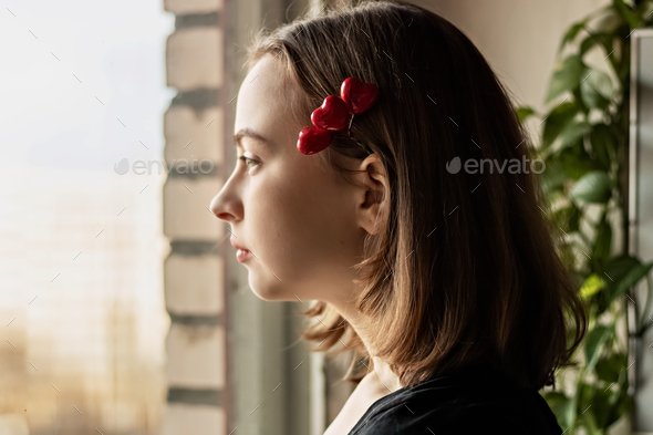Portrait of a beautiful sad girl looking out the window with hope and ...