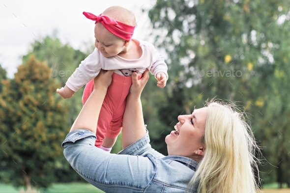 A young woman with blonde hair throws a baby over her head.Mom and ...