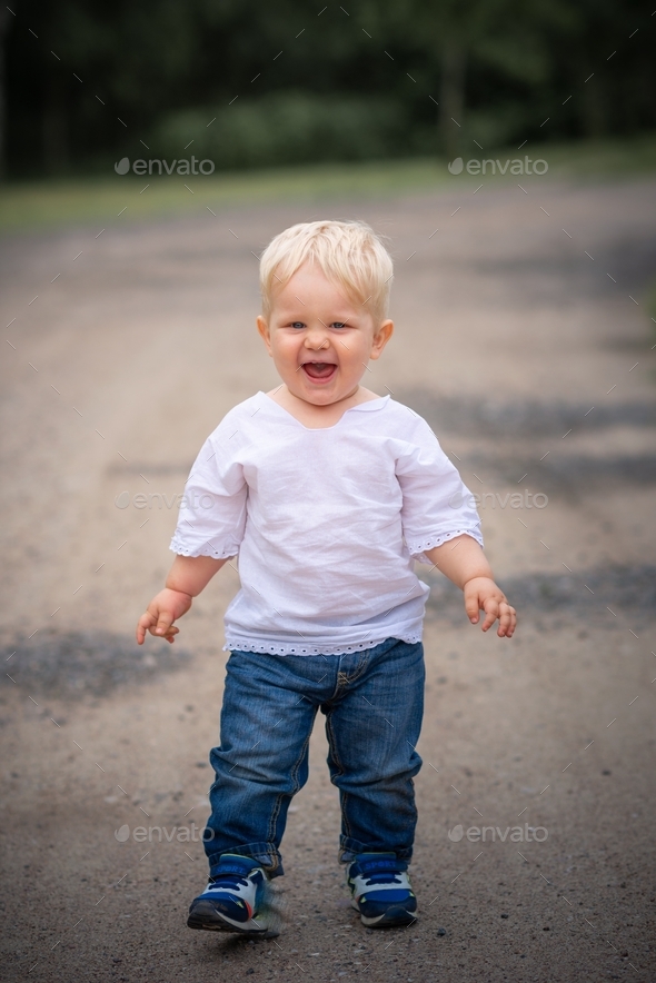 little boy in jeans and a white shirt on a walk in the summer at sunset ...