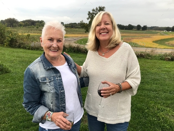 A baby boomer woman drinks a glass of wine and laughs with her senior ...