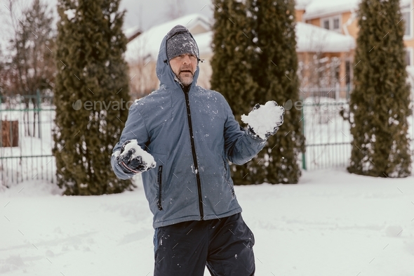 A man throws snowballs in the yard of a private house on a frosty day ...