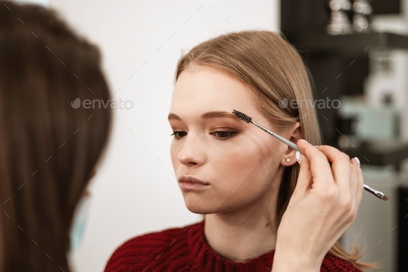 makeup artist applies eyebrow shadow on a beautiful young woman blonde ...