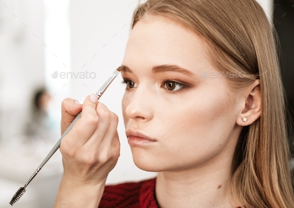 makeup artist applies eyebrow shadow on a beautiful young woman blonde ...