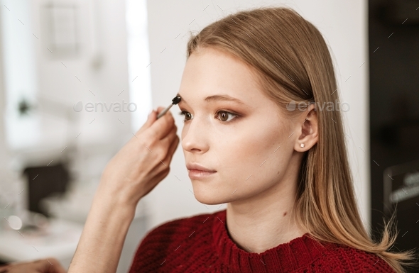 makeup artist applies eyebrow shadow on a beautiful young woman blonde ...