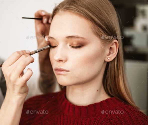 makeup artist applies eye shadow to the eyelids on a beautiful young ...