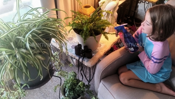 Generation z girl uses water mister to water house plants in living ...