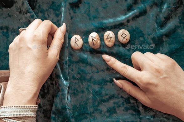 stone runes in the hands of a young woman and candles on a blue velvet ...