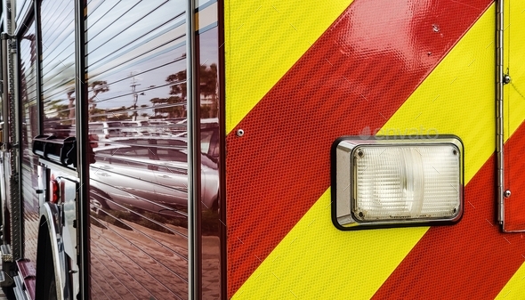 Fire truck from behind in red with yellow stripes and reflections of ...
