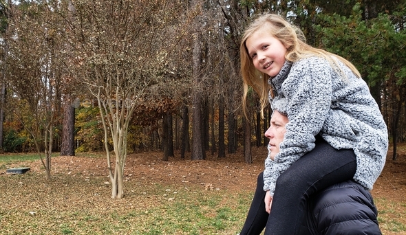Daughter traveling piggyback on her dads shoulders through a city park ...