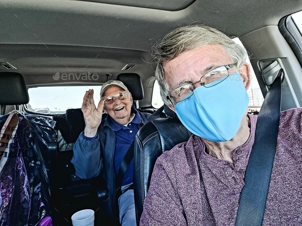 Active baby boomer son with face mask driving his senior dad back home ...
