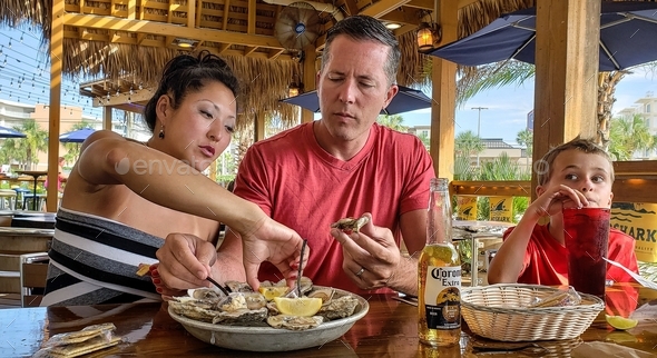 Generation X couple eating raw oysters at beach restaurant with ...