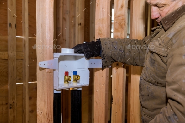 Plumber installing laundry outlet boxes with new home supplies Stock ...