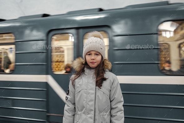 Little girl on a subway platform on the background of a passing train ...