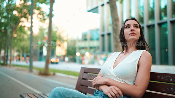 Beautiful woman sits on bench and looks around. Cute girl is sitting ...
