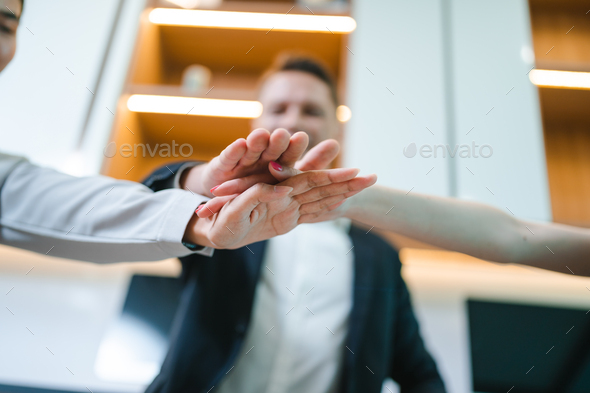 Team of young male and female employees stacking hands on top of each ...