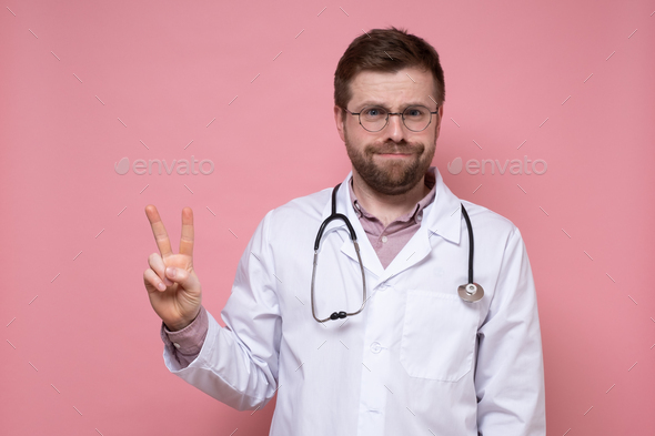 Tired male doctor with a stethoscope shows a symbol of victory. Gesture ...