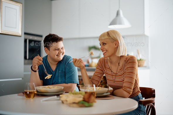 Happy female couple talking while eating lunch at dining table. Stock ...