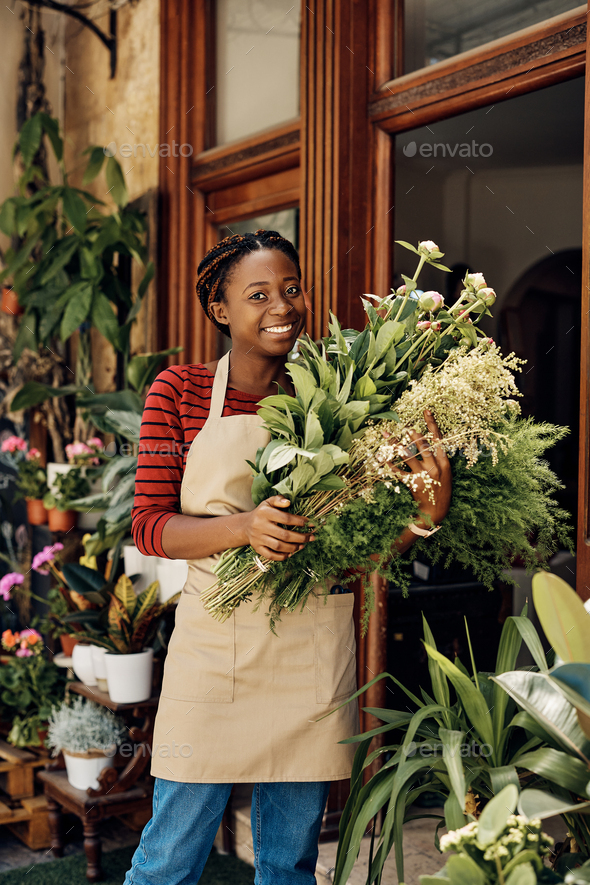 Happy black flower shop owner in front of her store looking at camera ...