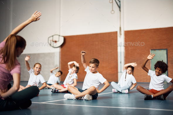 Elementary school children exercising with PE teacher at school gym ...