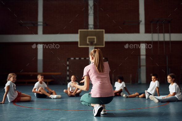 Rear view of PE teacher talking to group of kids during exercise class ...