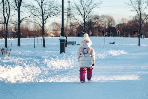 Little girl walking from behind in winter snowy public park in warm ...