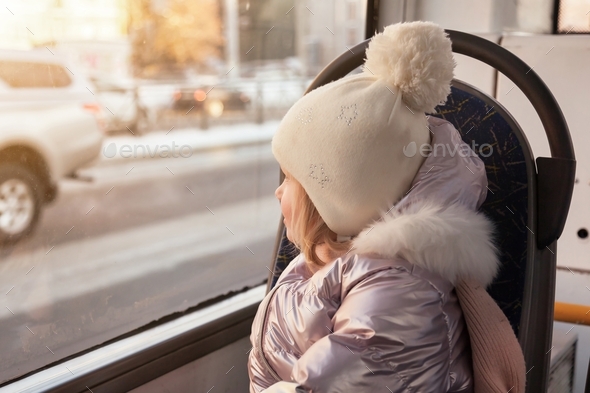 Little girl in bus watching on car at window of public city transport ...