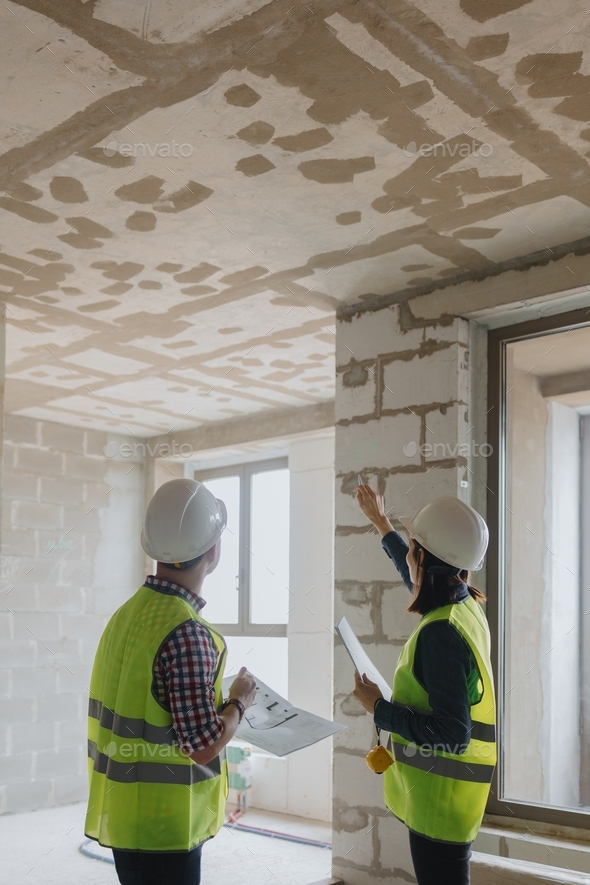 two engineers in white helmets and protective signal vests look at the ...