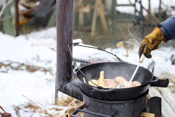 cooking chicken stew in winter in a cast iron cauldron in the open air ...