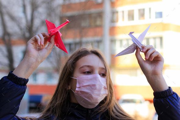 Pink and white origami paper cranes in the hands of a teenage girl in a ...