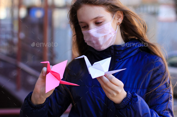 Pink and white origami paper cranes in the hands of a teenage girl in a ...
