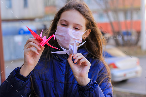 Pink and white origami paper cranes in the hands of a teenage girl in a ...