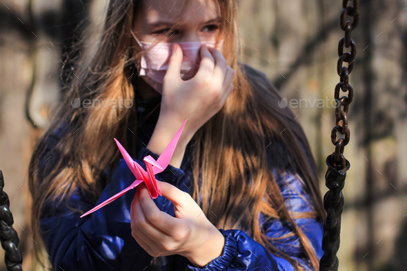 Pink and white origami paper cranes in the hands of a teenage girl in a ...