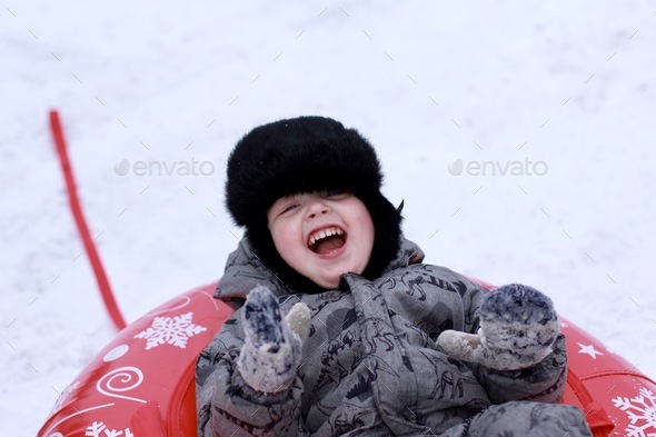 handsome little boy having fun on snow tube. Boy is riding a tubing ...