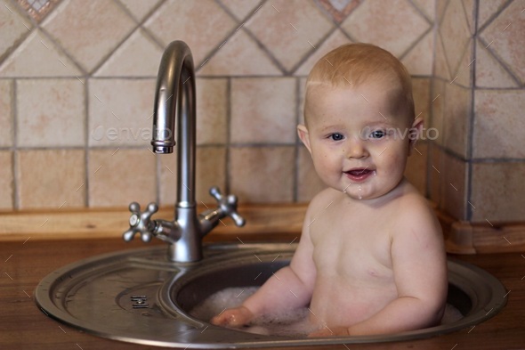 Baby boy having a bath in the kitchen sink. Happy childhood, child ...