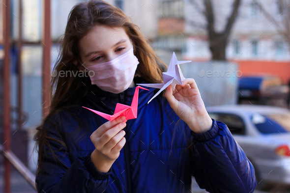 Pink and white origami paper cranes in the hands of a teenage girl in a ...