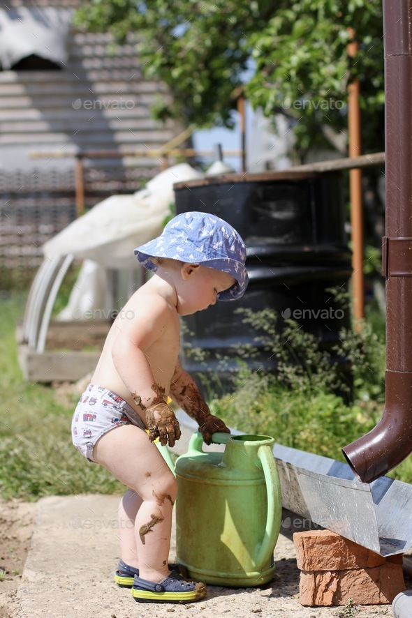 Cute little boy outdoor in the backyard. Kid watering plants at summer ...