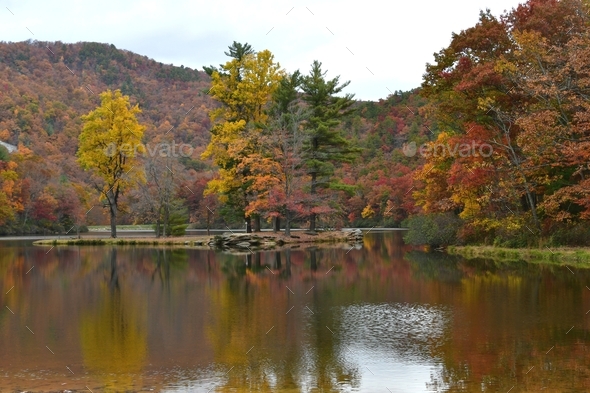 Trees on an island with colorful fall foliage reflecting in a mountain ...
