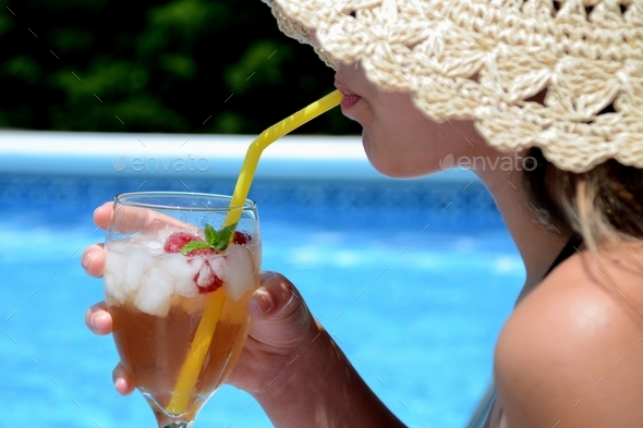 Female with long hair, dark tan and floppy straw hat enjoying a cold ...