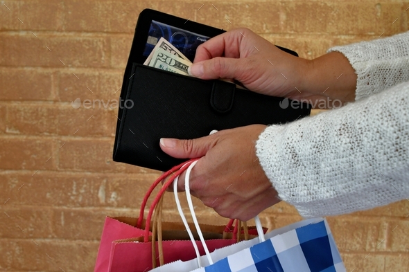 Pulling money out of a wallet while holding shopping bags to make a ...