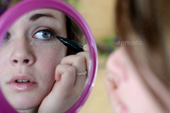 A young preteen tween teen carefully applying eye makeup eyeliner while ...