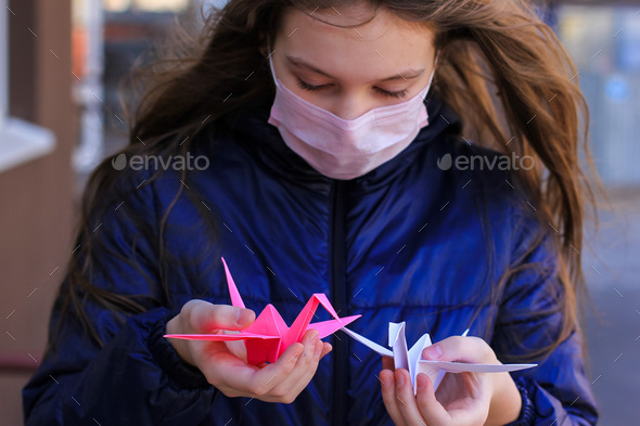 Pink and white origami paper cranes in the hands of a teenage girl in a ...